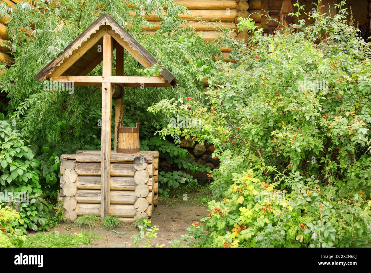 Log well with bucket and wooden carved decorations stands among green ...