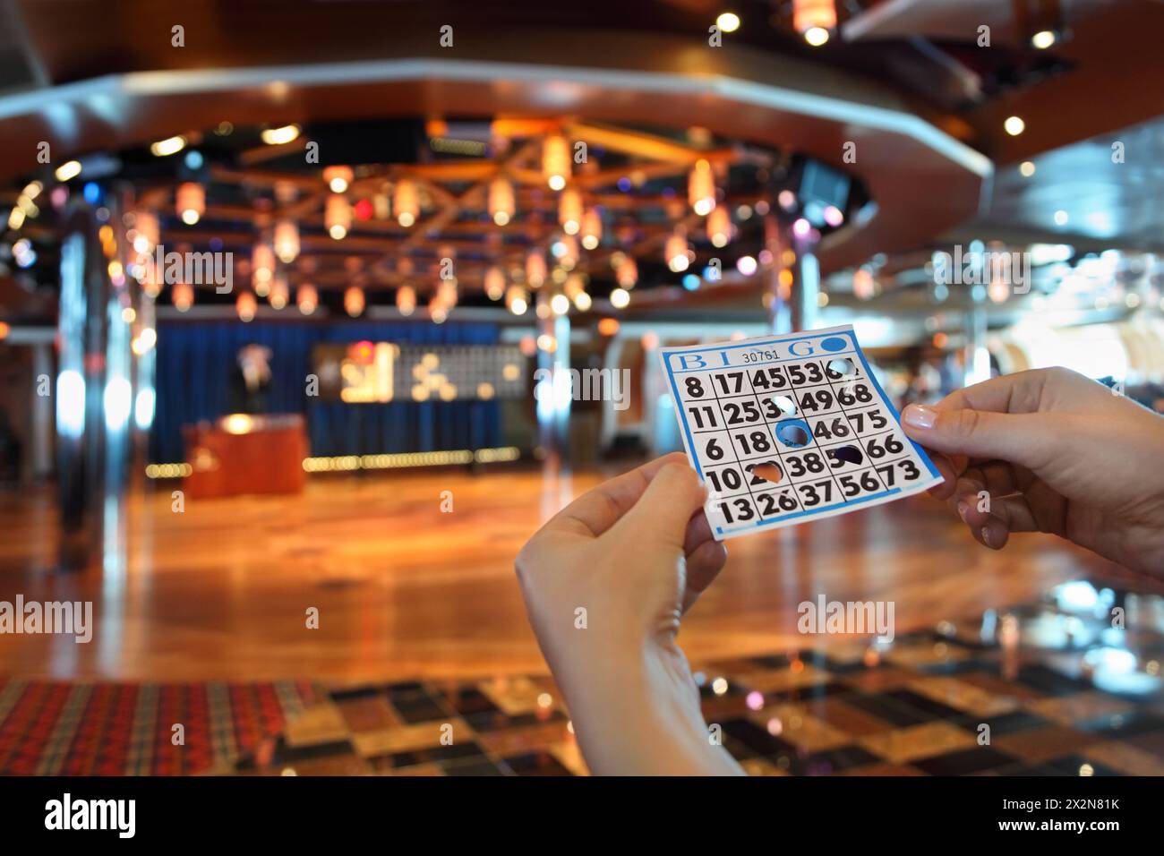 Female hands hold bingo card with holes at background of big board ...