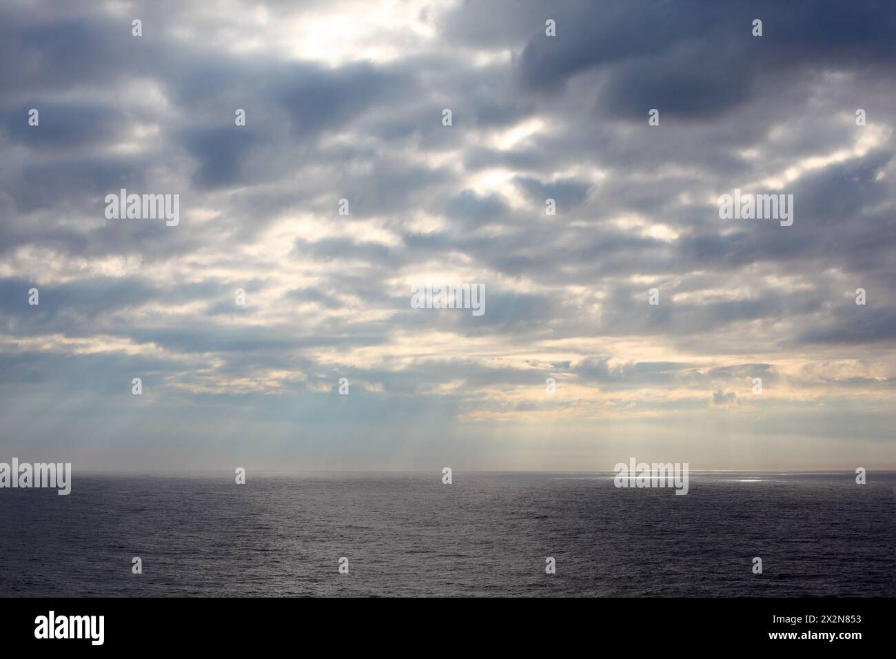 gray clouds over dark and cold sea; rays of sun breaks through clouds ...