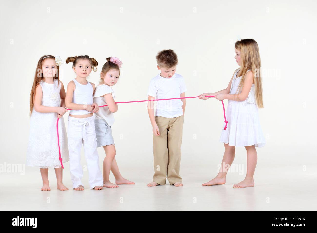 Four little girls in white clothes draw over pink rope and boy looks at ...