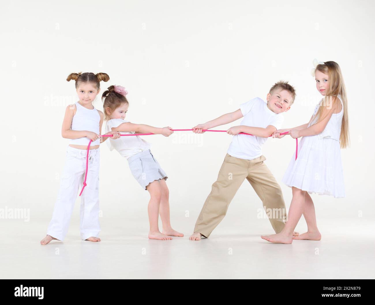 Four happy and cute little children in white pull pink rope Stock Photo ...