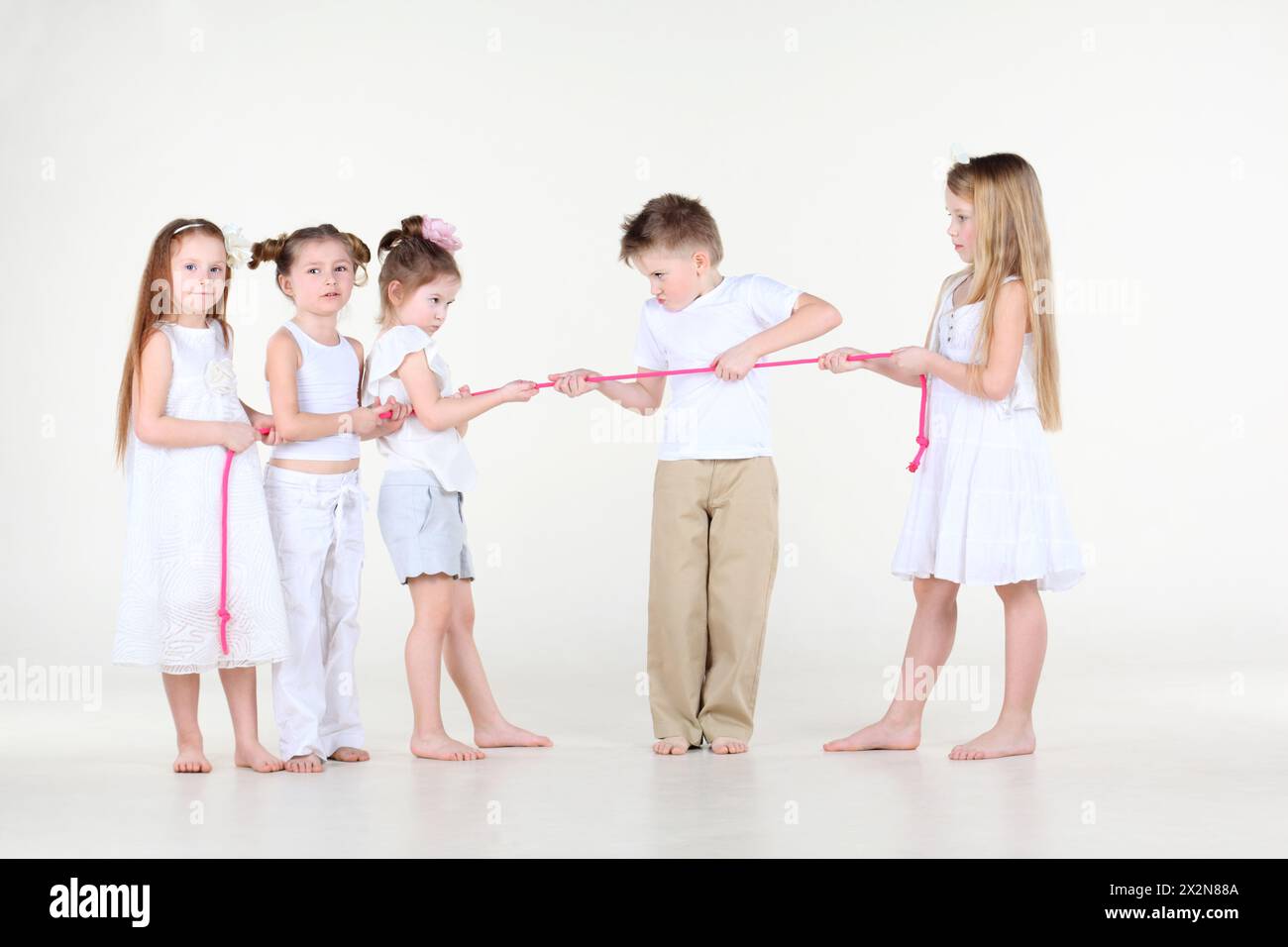 Five strained little children in white clothes draw over pink rope ...