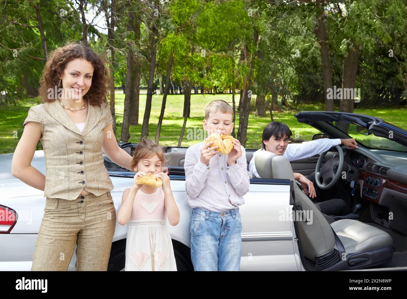 Mother with son and daughter stand near open top car, children eat ...