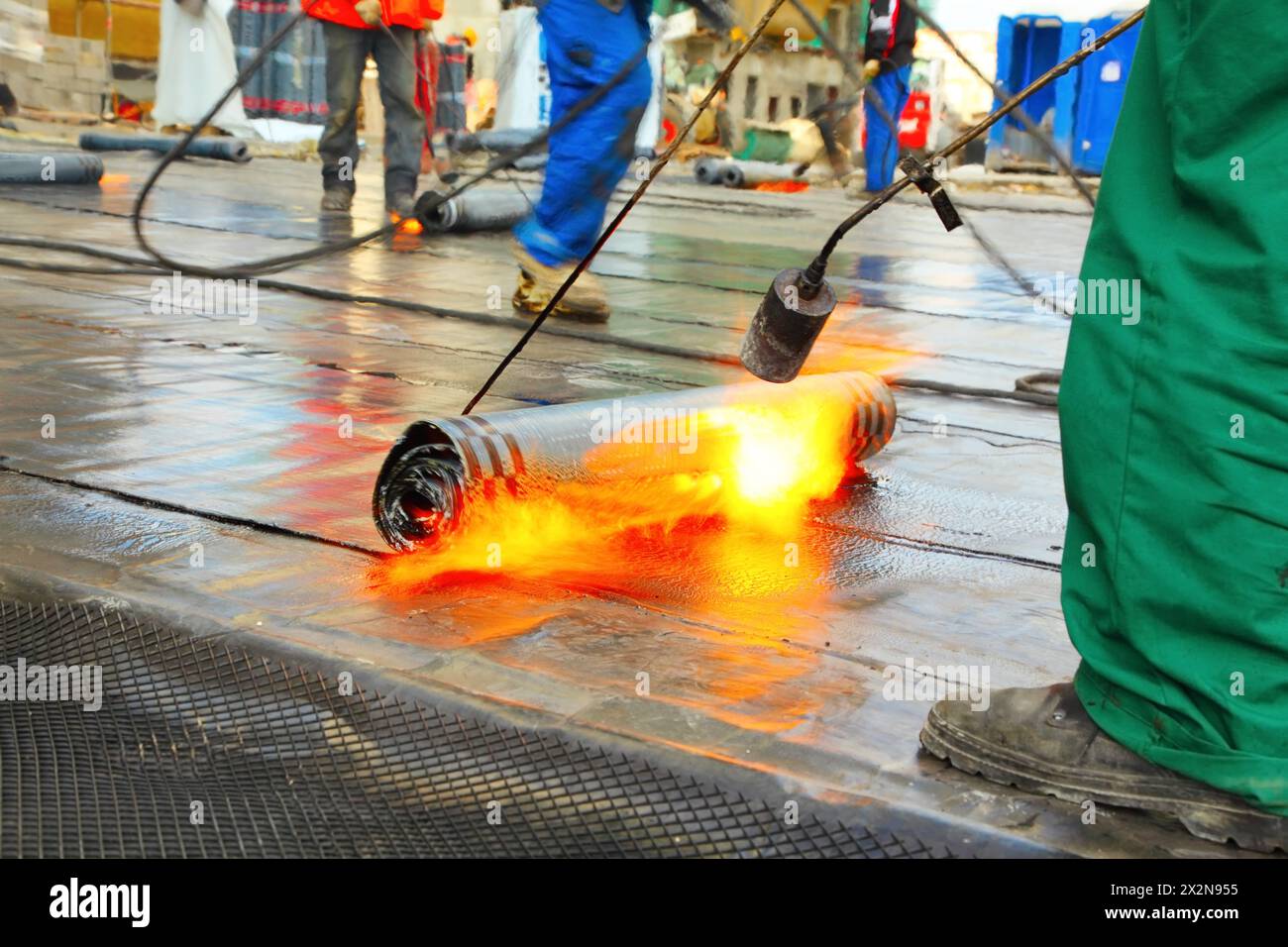 men in green, blue pants crout roof with hot tar Stock Photo - Alamy