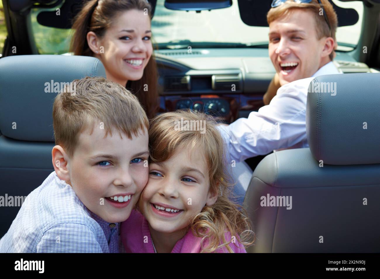 Laughing little brother and sister sit on back seat of open top car ...