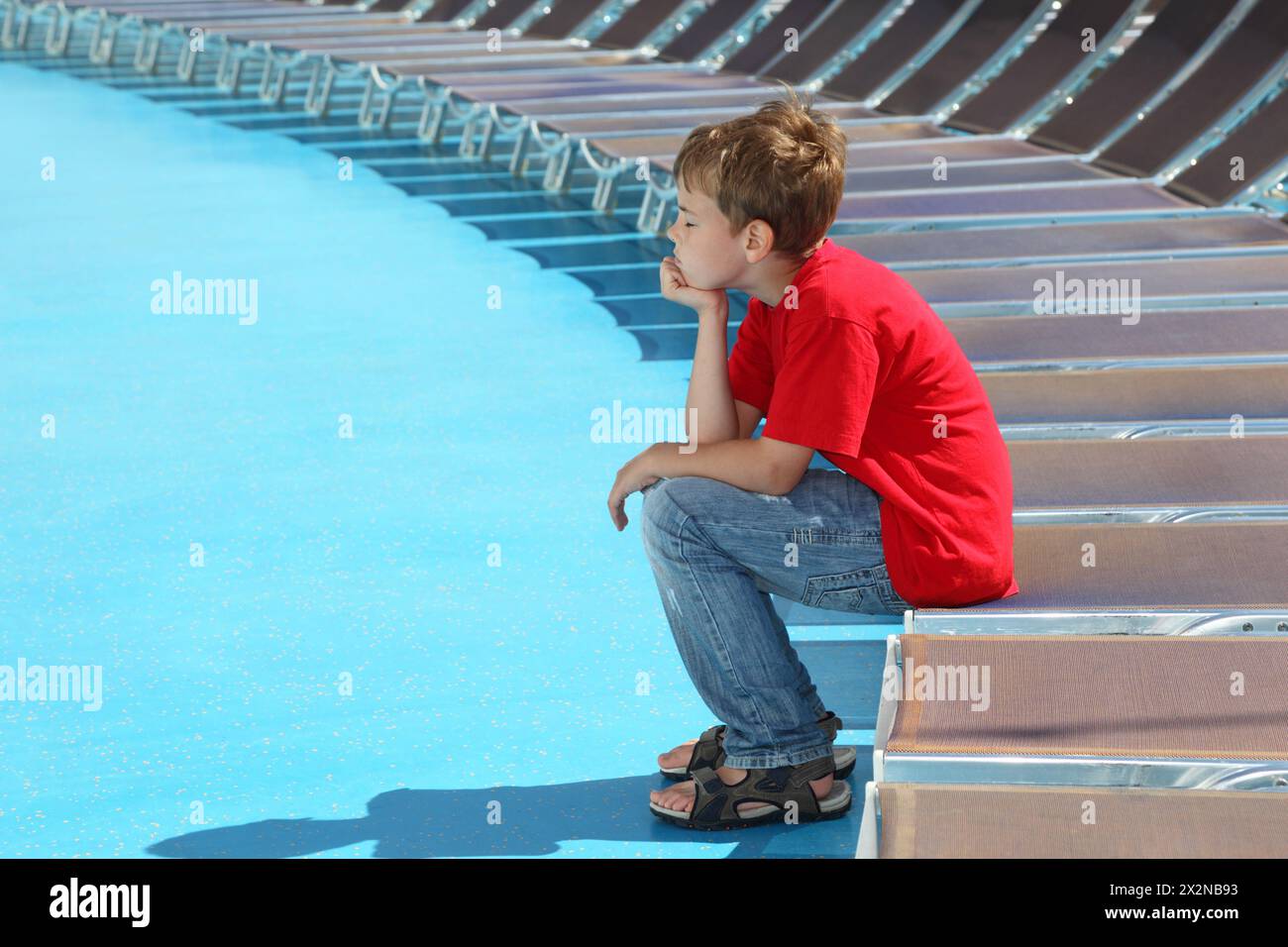 Tired boy sits on edge of deck-chair on blue deck of cruise liner Stock ...