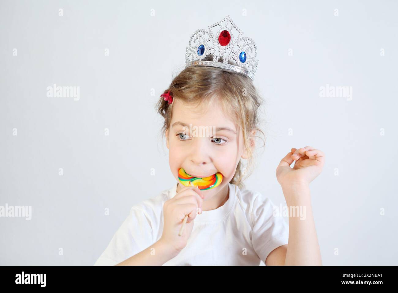 Little girl in white t-shirt and shiny princess crown eats colorful ...