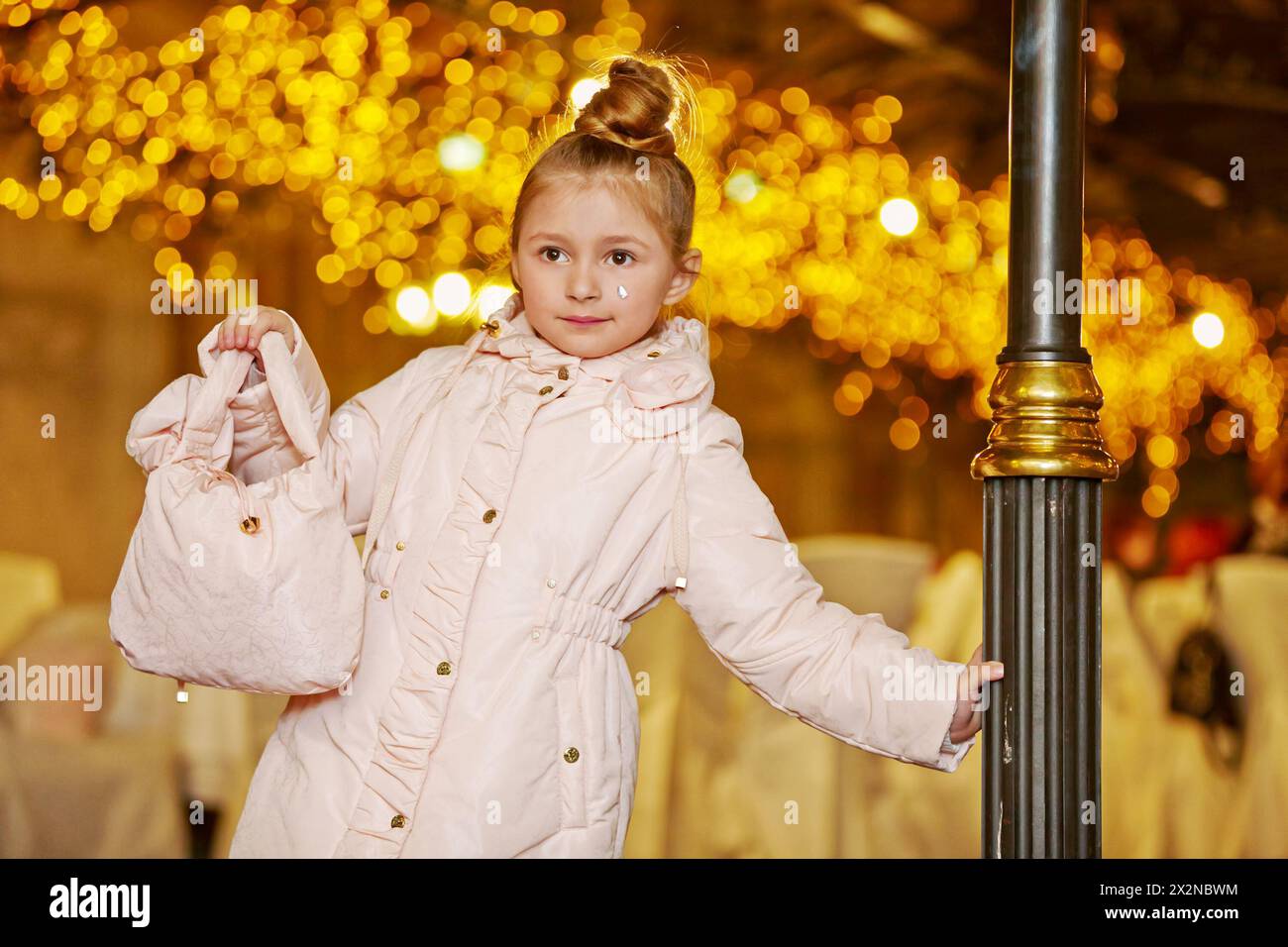 Girl in light coat stands, leaning one hand on decorative lamp post ...