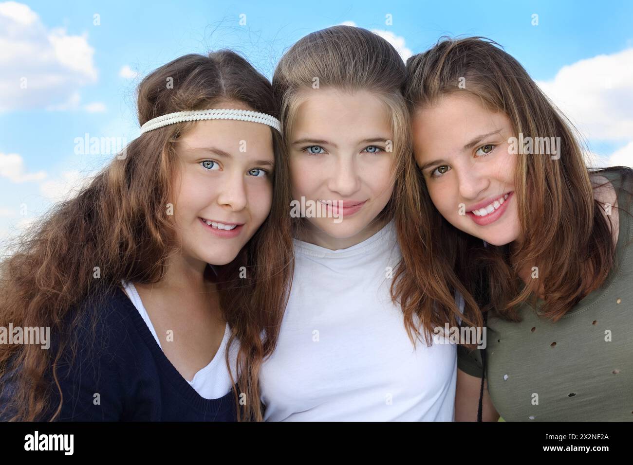 Three smiling girls hug at background of blue sky with white clouds ...