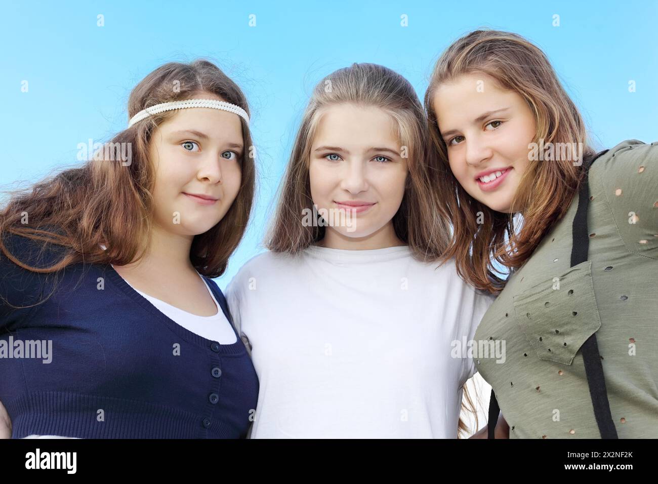 Three happy girls hug at background of blue sky. Friendship forever ...