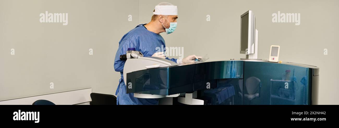 A man in a surgical suit stands before a desk with a monitor Stock ...