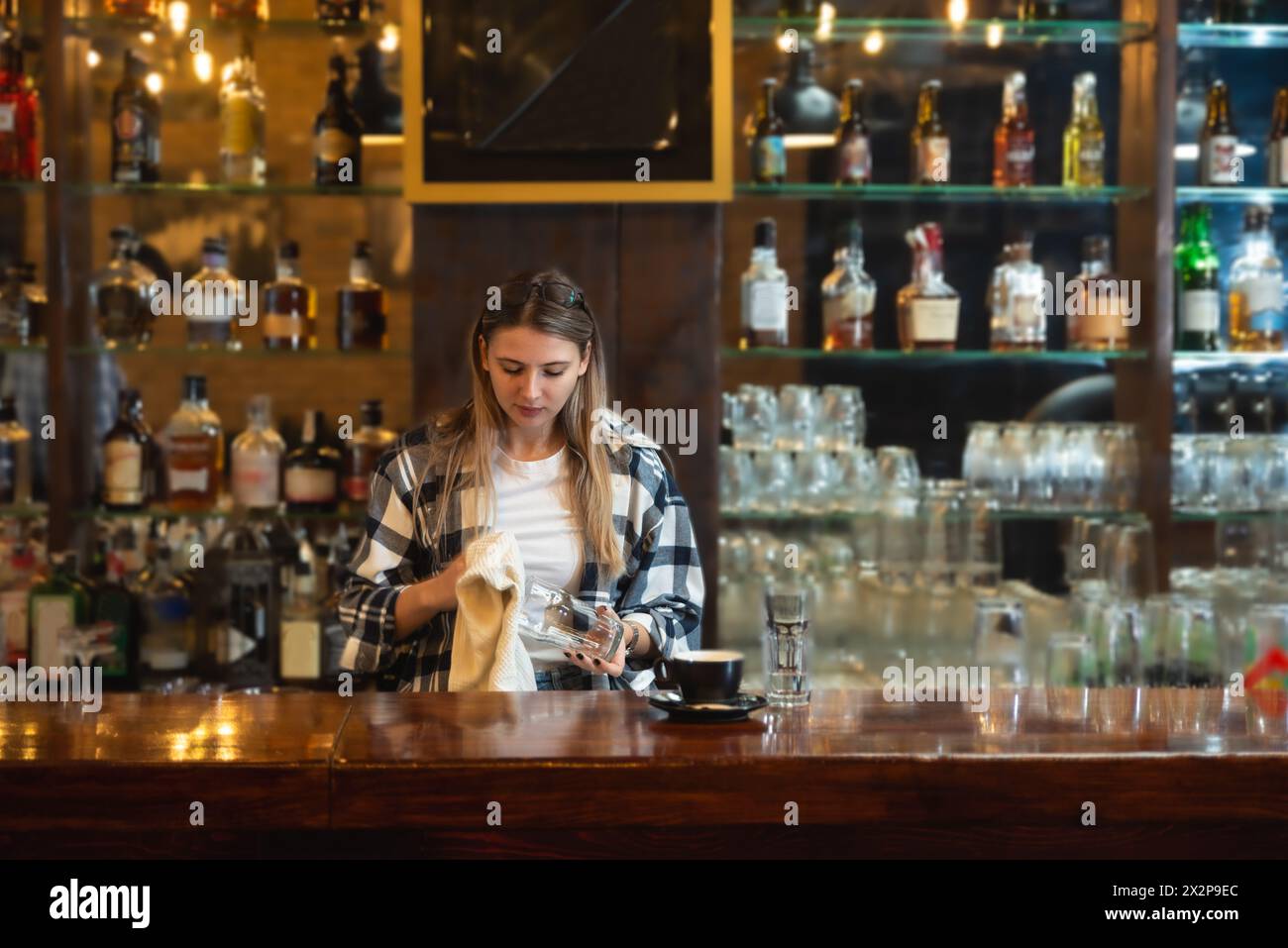 Waitress standing in bar and wiping and polishing beer glass. Bartender ...