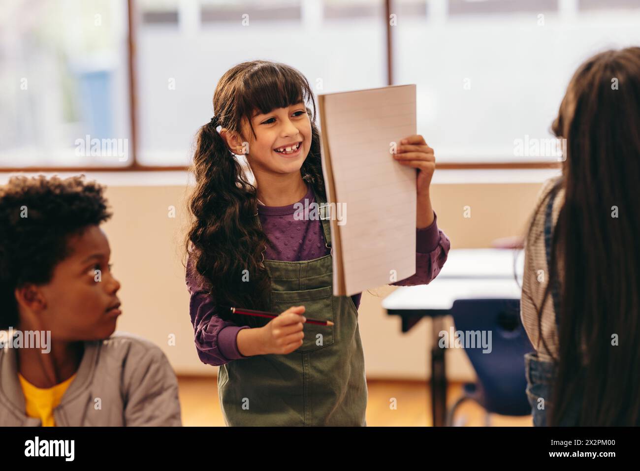 Happy young girl holding up a blank drawing book in an art class ...
