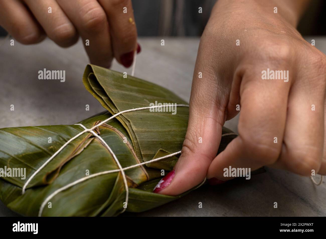 Woman's hands tying a hallaca or tamale in a banana leaf. Traditional ...