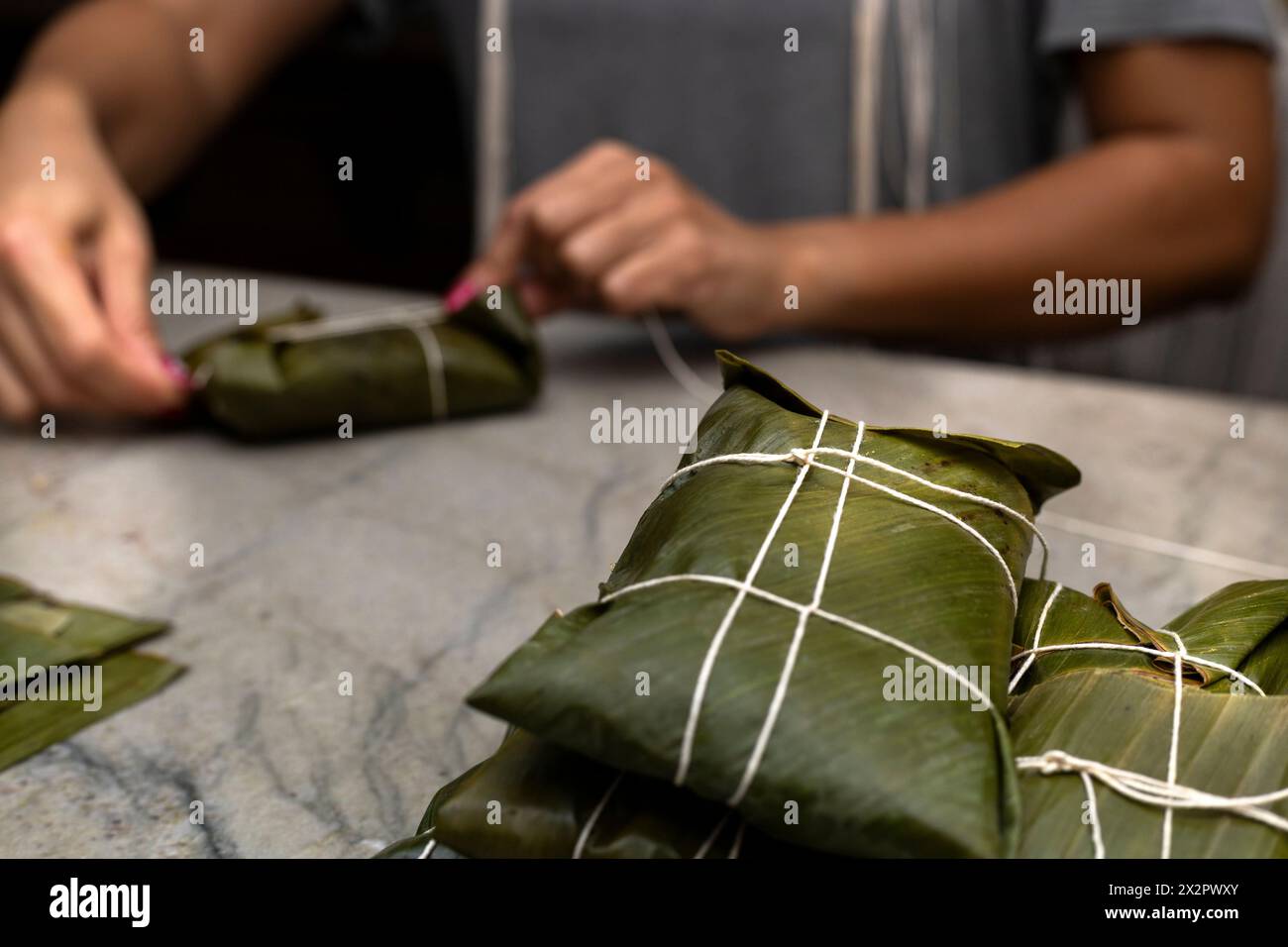 Woman's hands tying a hallaca or tamale in a banana leaf. Traditional ...