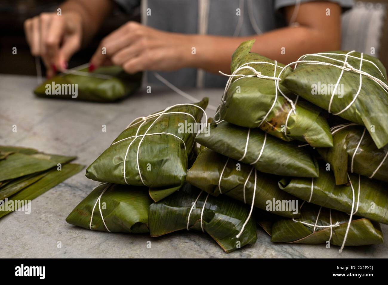 Woman's hands tying a hallaca or tamale in a banana leaf. Traditional ...