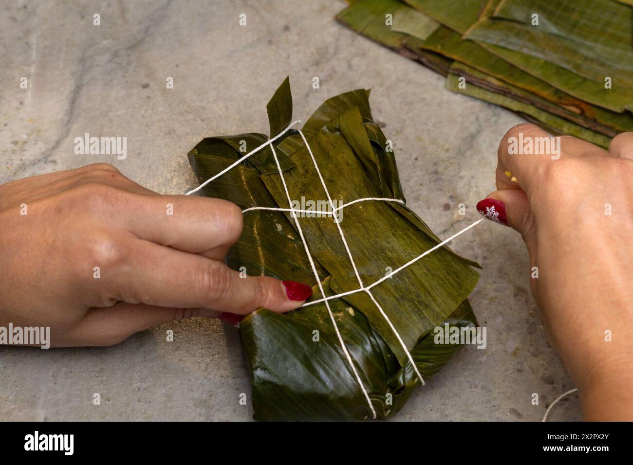 Woman's hands tying a hallaca or tamale in a banana leaf. Traditional ...