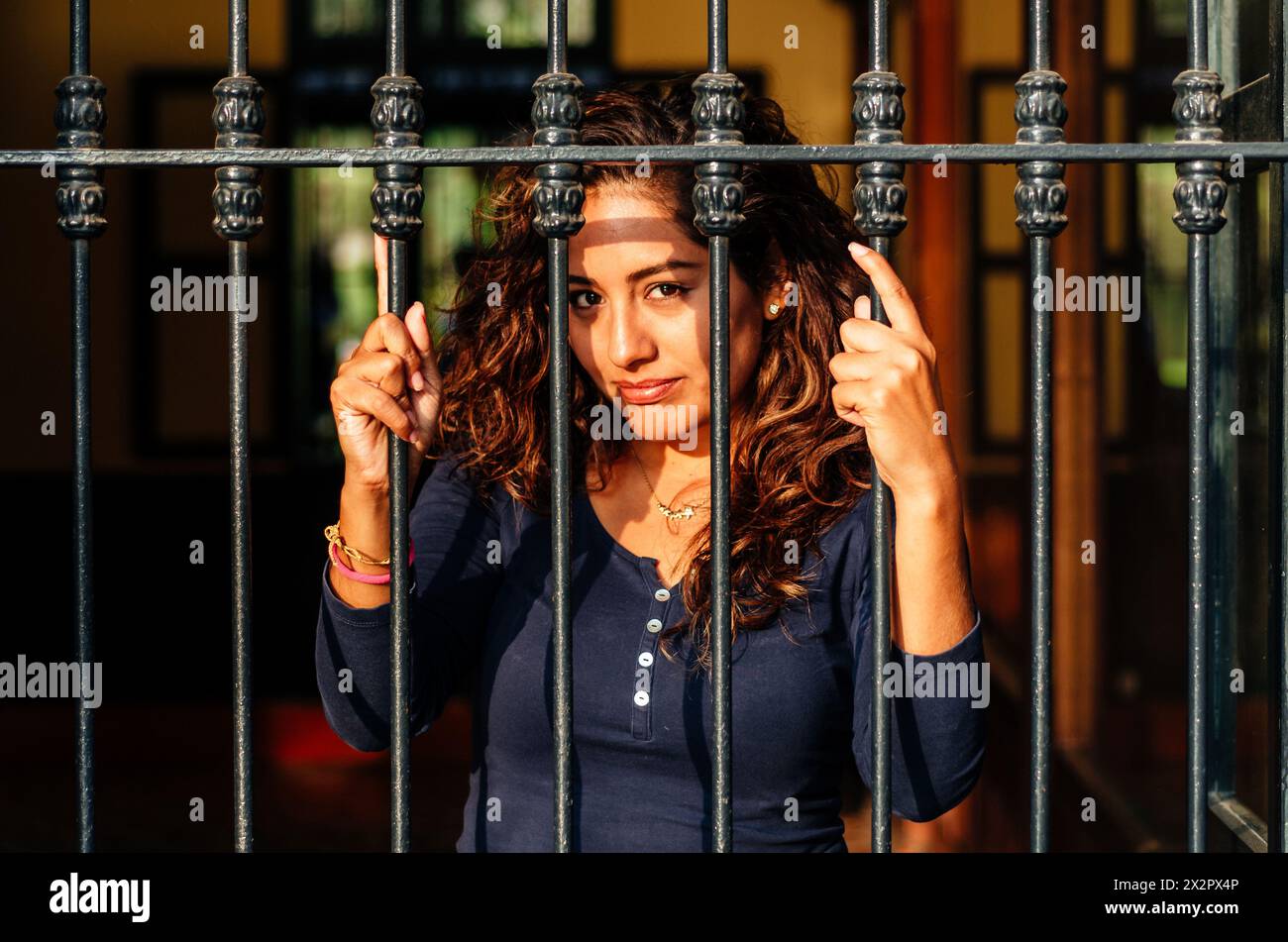 Warm portrait of a cheerful woman standing behind a gate at golden hour ...