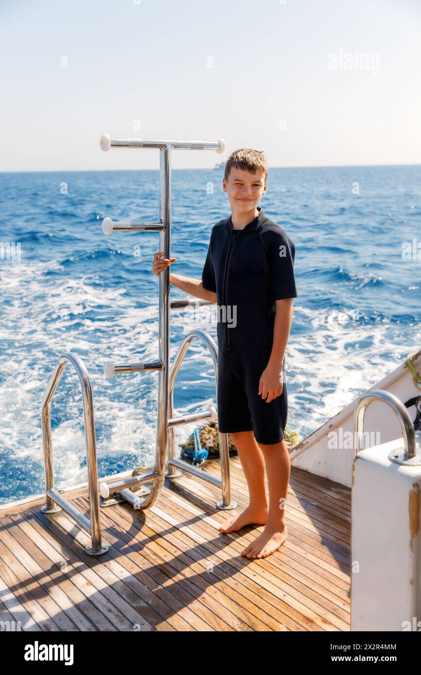A 14-year-old boy in a diving suit stands on the stern of a yacht Stock ...