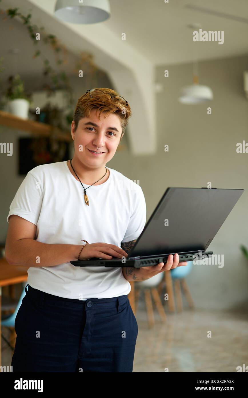 Confident transgender employee holds laptop in modern office cafe ...