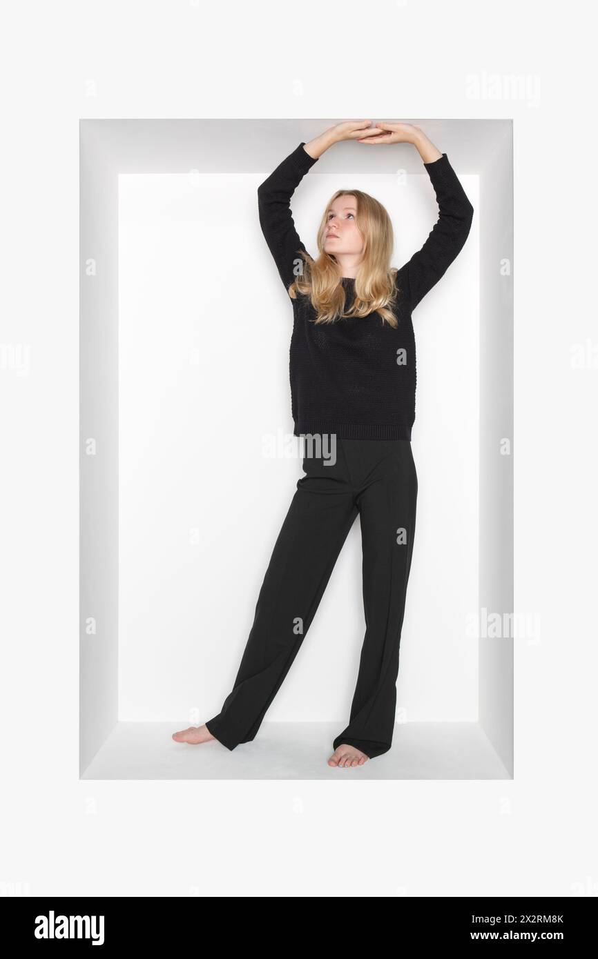 Thoughtful teenage girl with arms raised standing against white ...