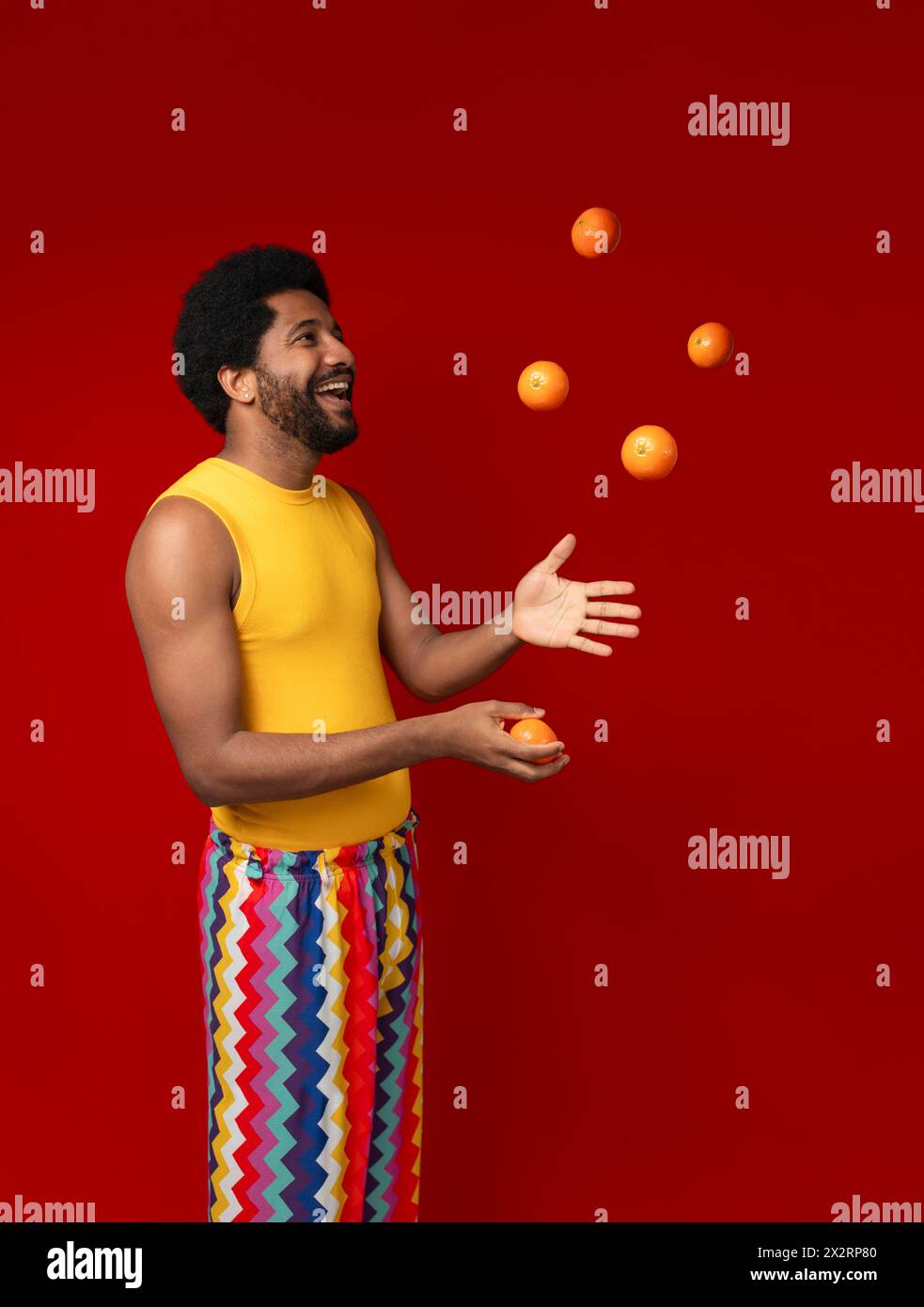 Happy man juggling with oranges against red background Stock Photo - Alamy