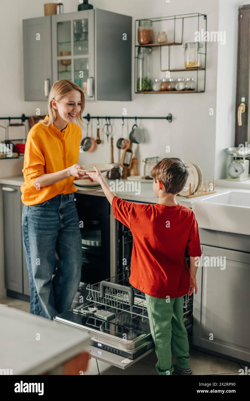 Boy helping mother in washing plates using dishwasher at home Stock ...