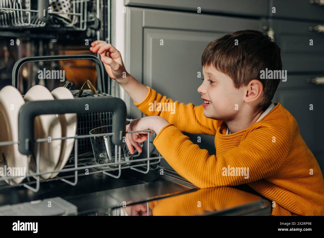 Smiling boy near dishwasher with plates in kitchen at home Stock Photo ...