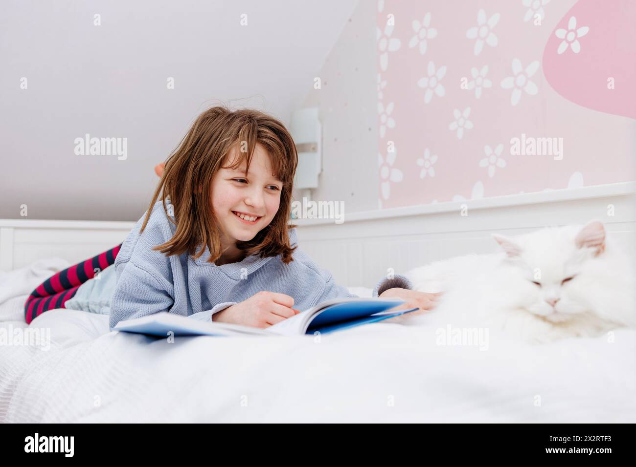 Happy girl lying on bed and reading book near cat at home Stock Photo ...
