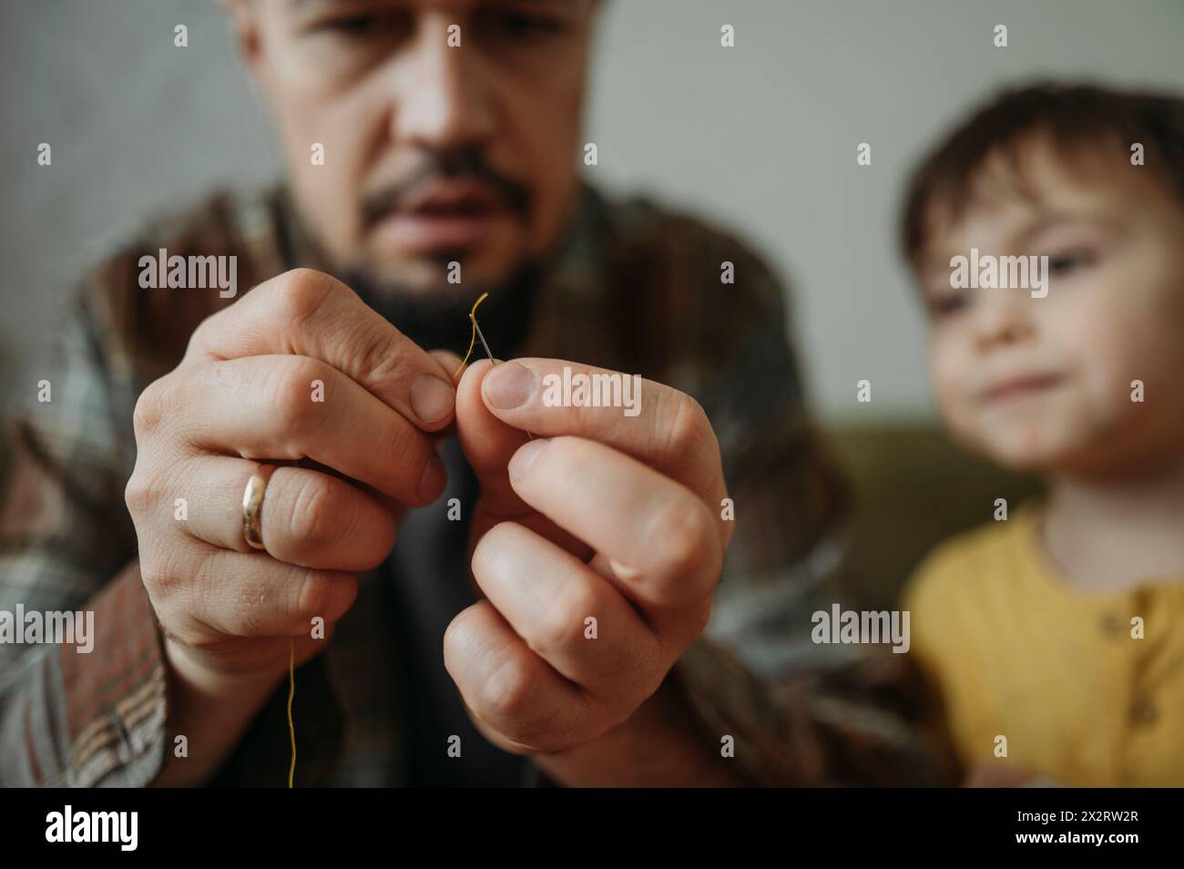 Boy with father trying to put thread in needle at home Stock Photo - Alamy