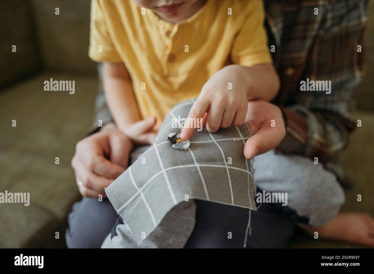 Father with son learning to sew button on gray colored cloth at home ...