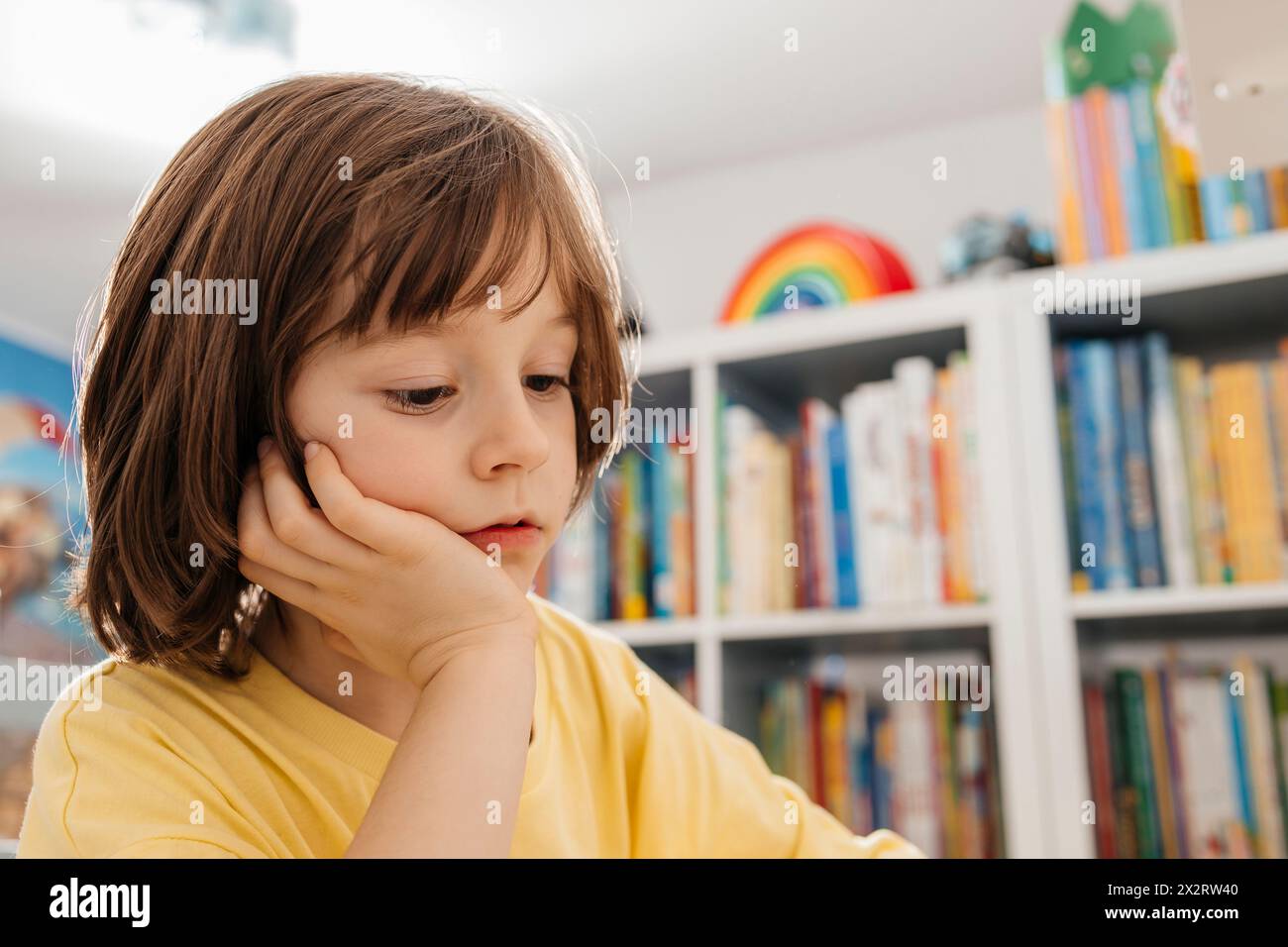 Sad boy resting head on hand in front of bookshelf Stock Photo - Alamy