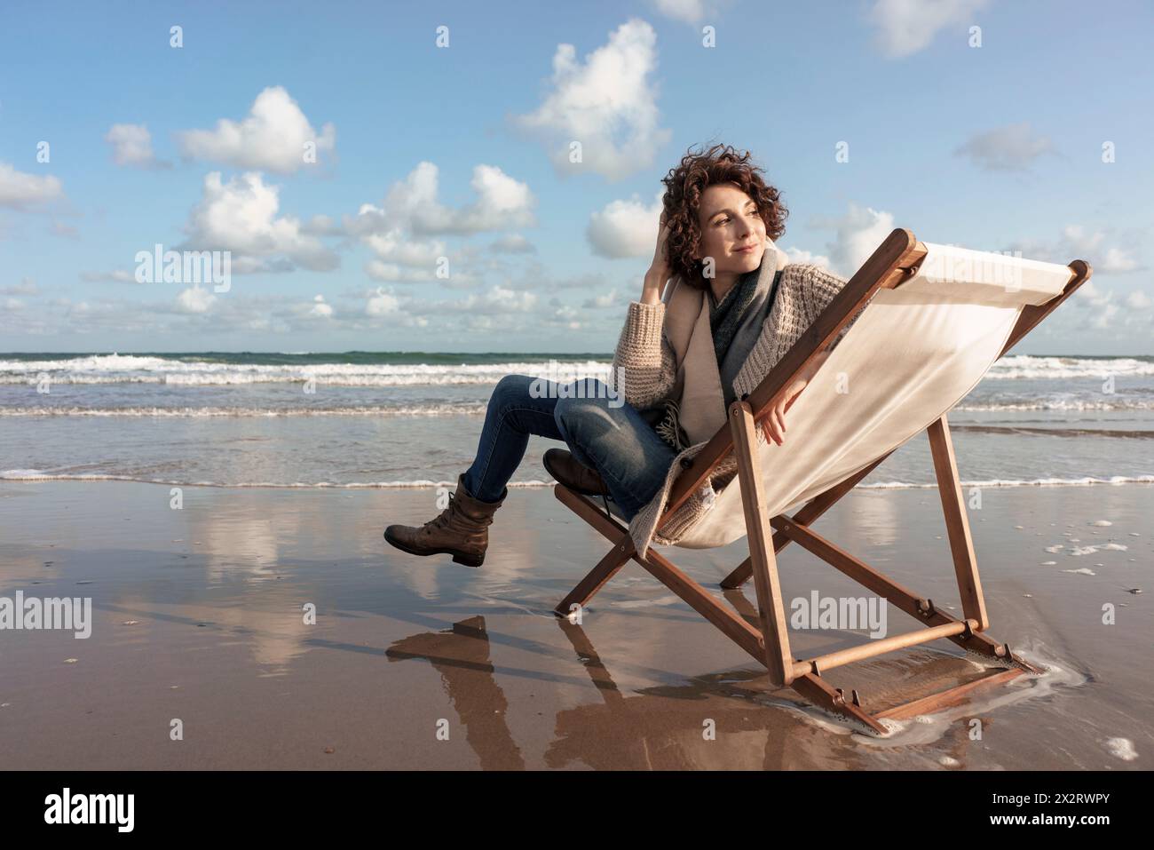 Smiling woman sitting on deck chair day dreaming at beach Stock Photo ...