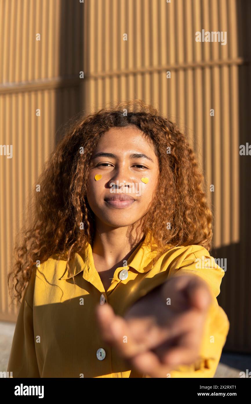 Beautiful young woman with yellow heart shape stickers on cheeks giving ...