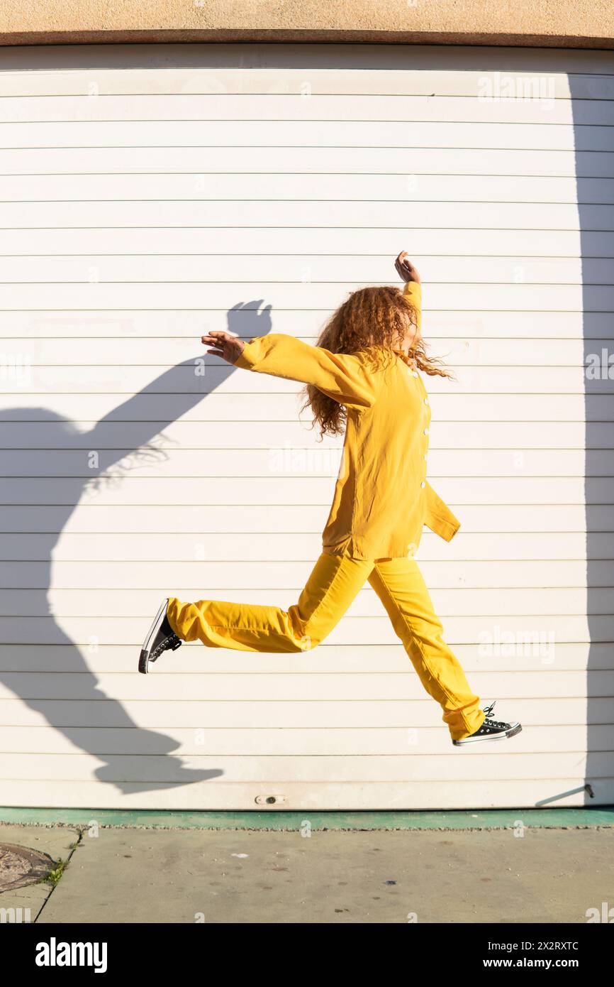 Excited young woman jumping in front of white shutter Stock Photo - Alamy