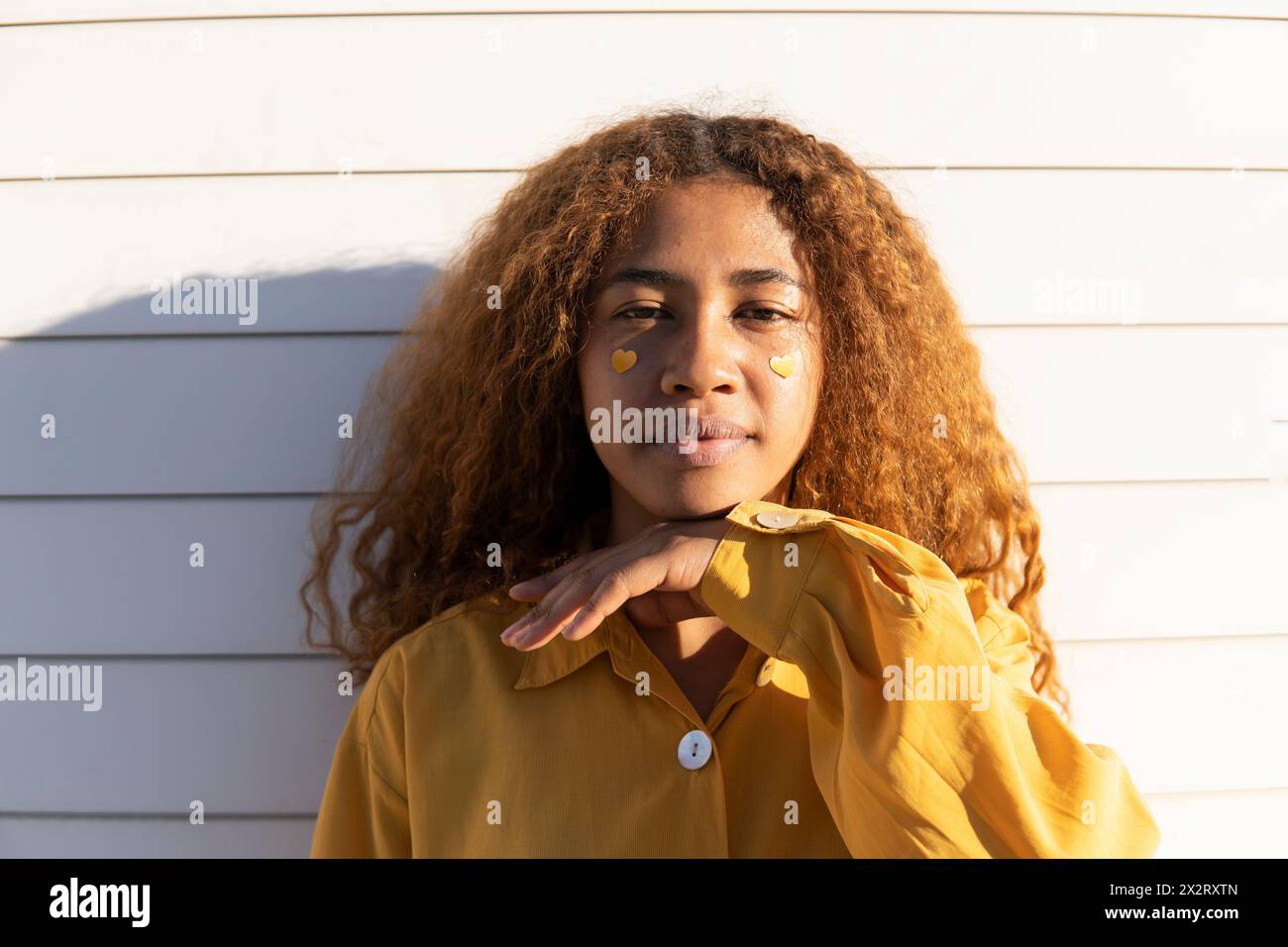 Curly haired woman with heart stickers on cheek in front of white ...