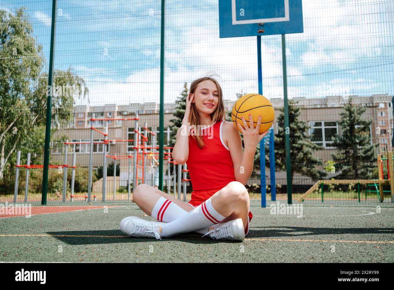 Basketball player sitting with ball on ground in schoolyard Stock Photo ...
