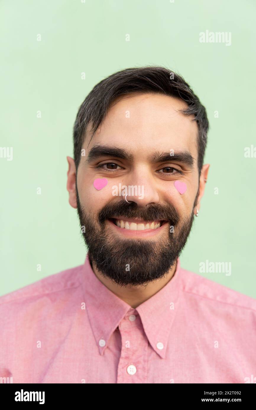 Happy man with pink heart shape stickers on cheeks against mint green ...