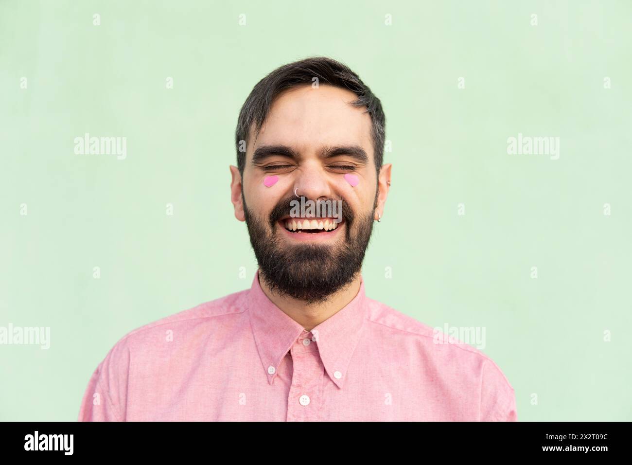 Cheerful man with pink heart shape stickers on cheeks against mint ...