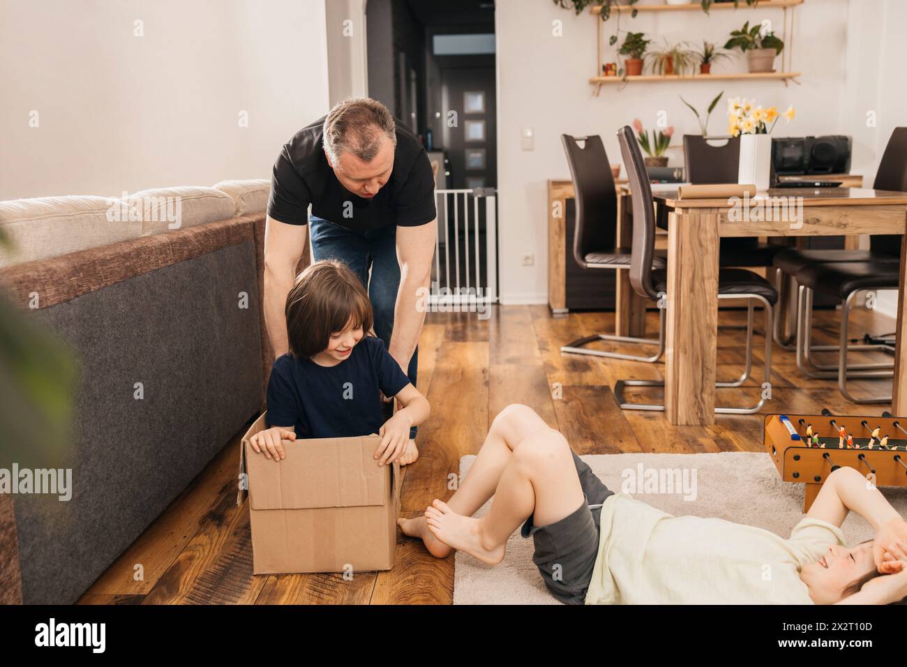 Happy boy lying near father pushing brother sitting in cardboard box at ...