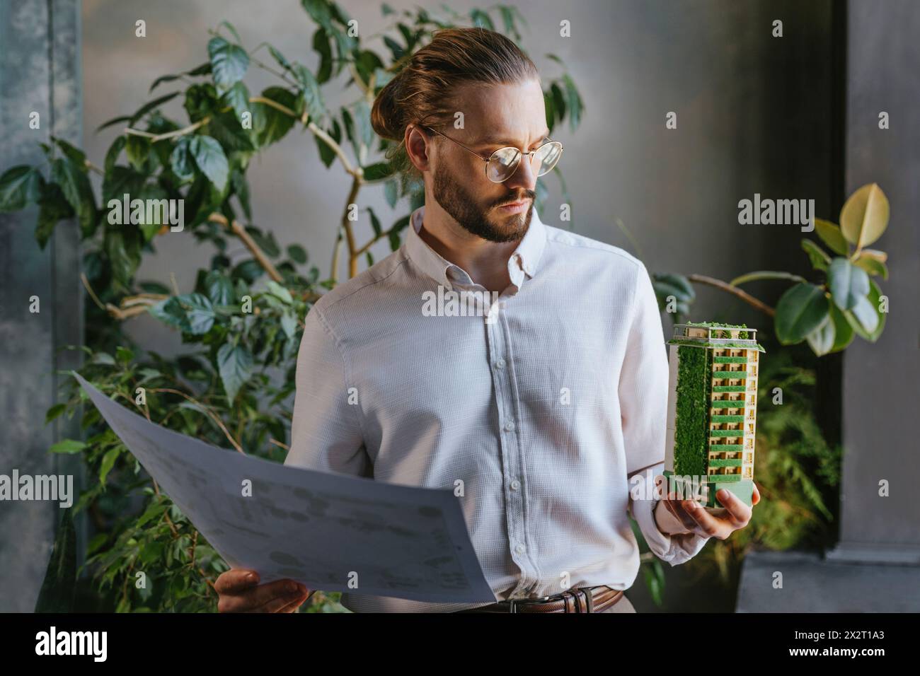 Architect holding blueprint and examining building model at office ...
