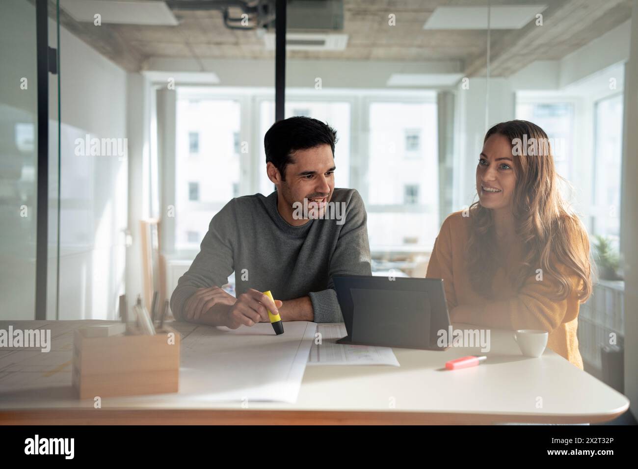 Smiling architects discussing with tablet PC and blueprints at desk ...