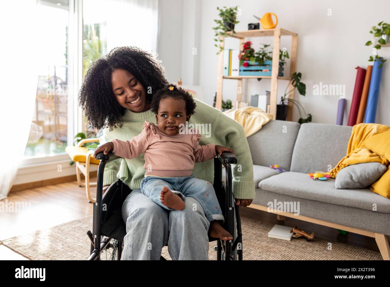 Cute baby girl sitting on young mother with disability in wheelchair at ...