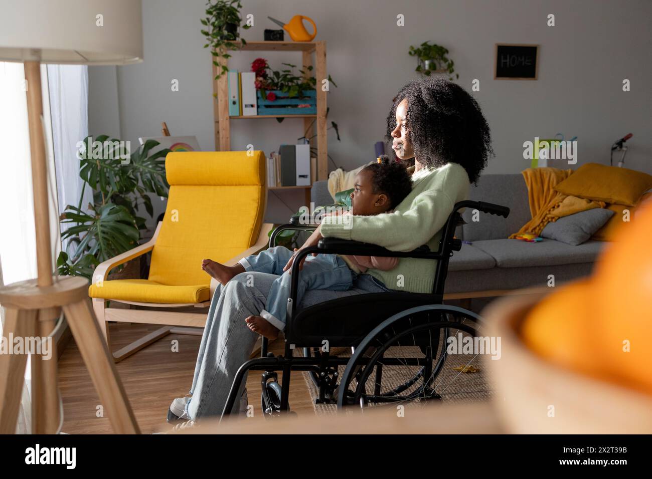Baby girl sitting on mother with disability in wheelchair at home Stock ...