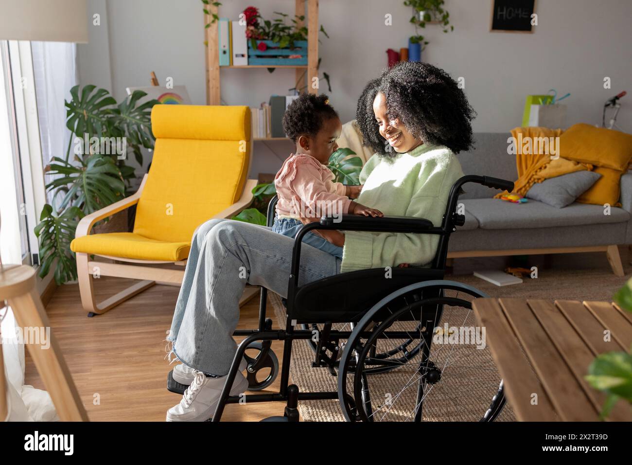 Baby girl sitting on smiling mother with disability in wheelchair at ...