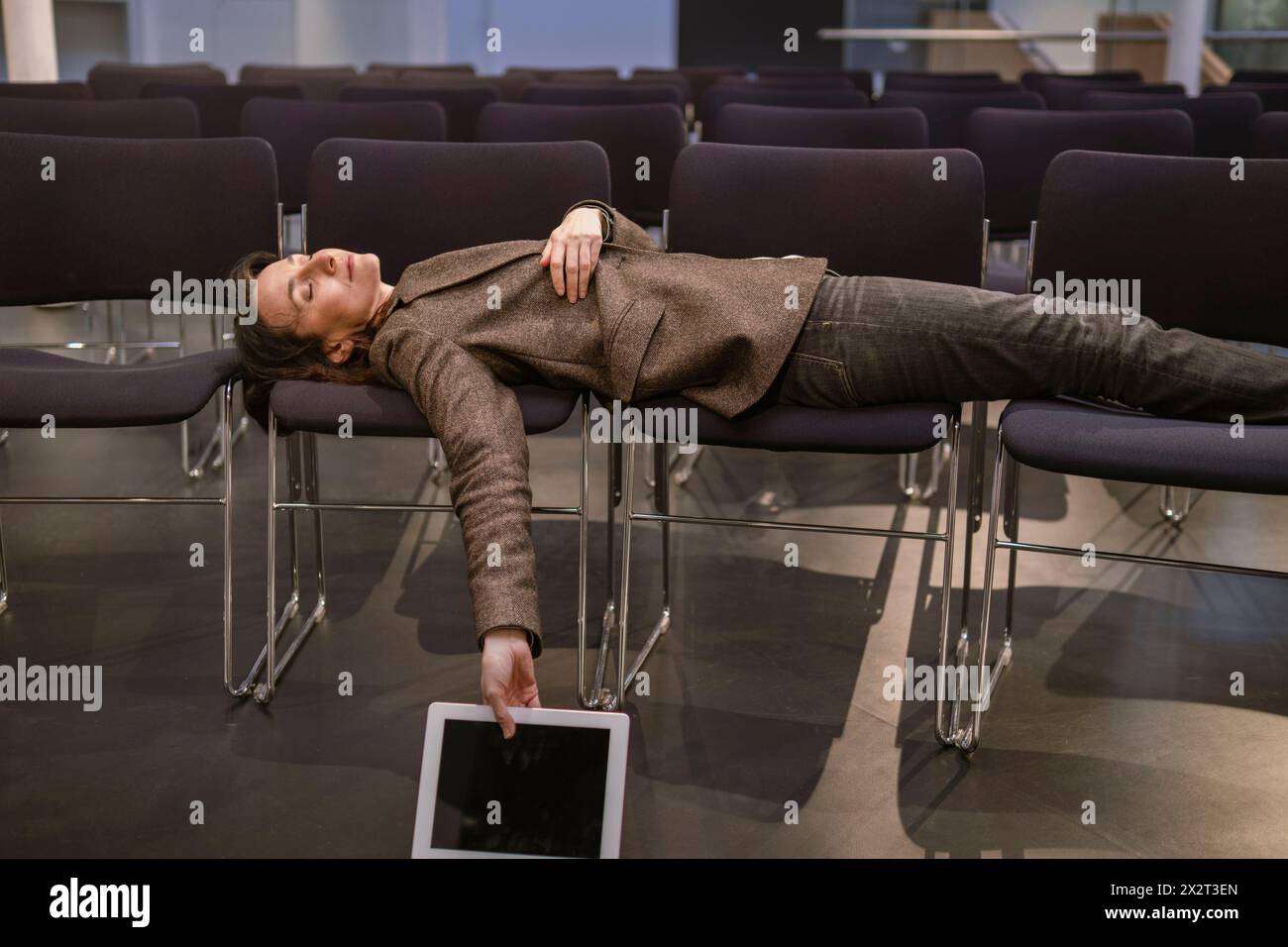 Tired professor holding tablet PC and sleeping on chairs in lecture ...