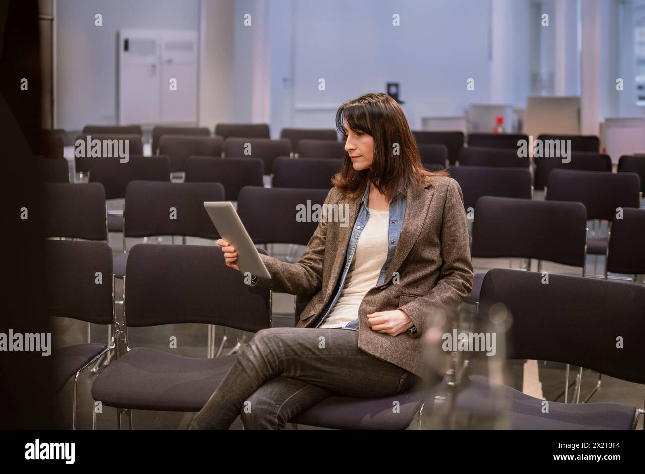 Mature professor using tablet PC sitting on chair in lecture hall Stock ...