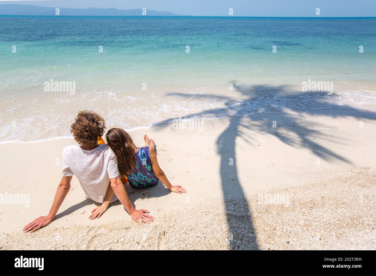 Couple looking at sea sitting on sand at beach Stock Photo - Alamy