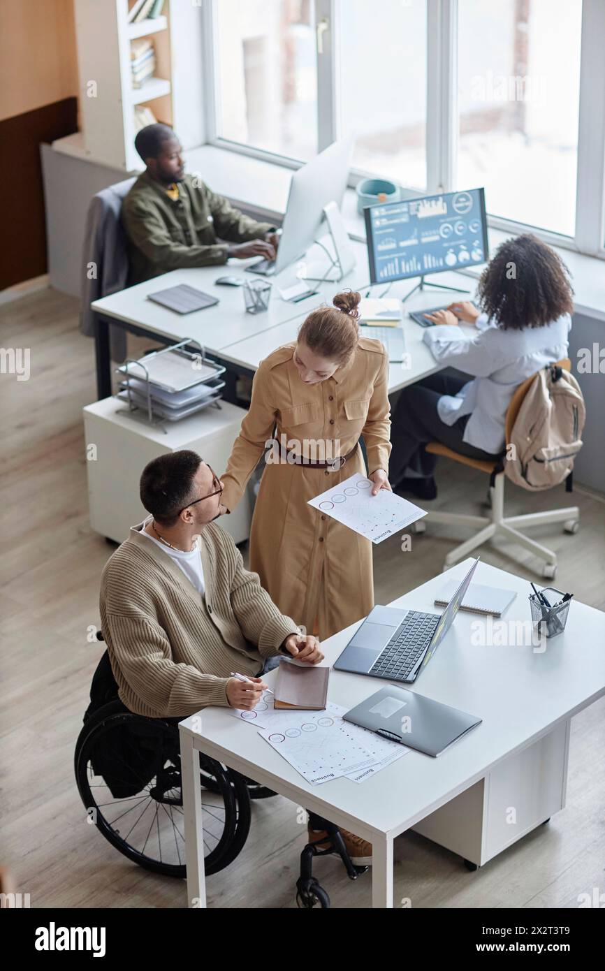 Manager taking help from IT professional sitting in wheelchair at desk ...