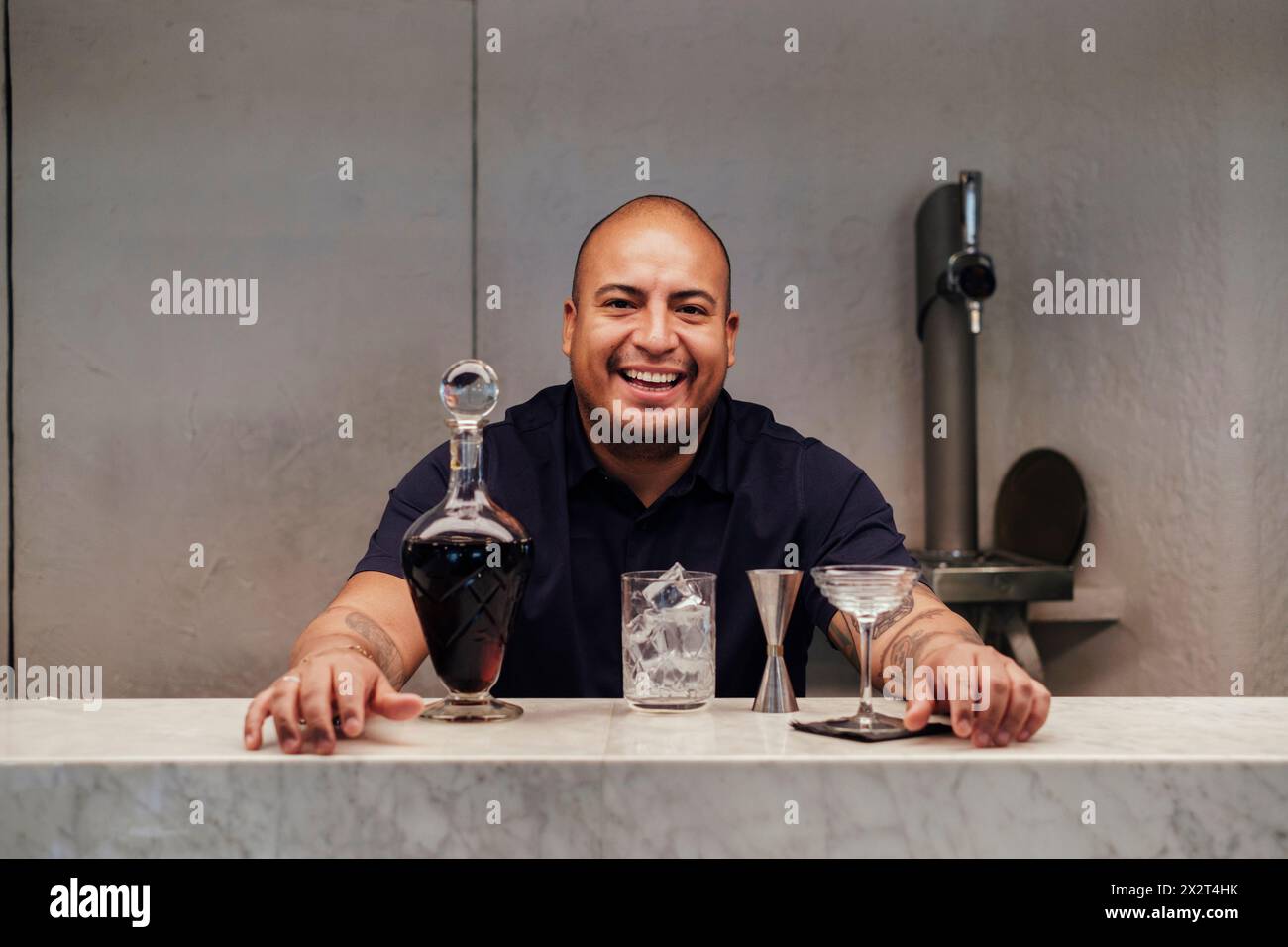 Smiling bartender with cocktail and alcohol bottle at bar counter in ...